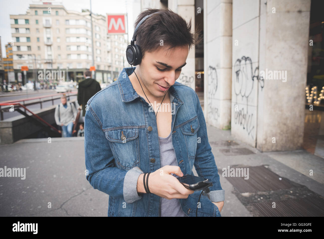 young handsome alternative dark model man outdoor in the city listening ...