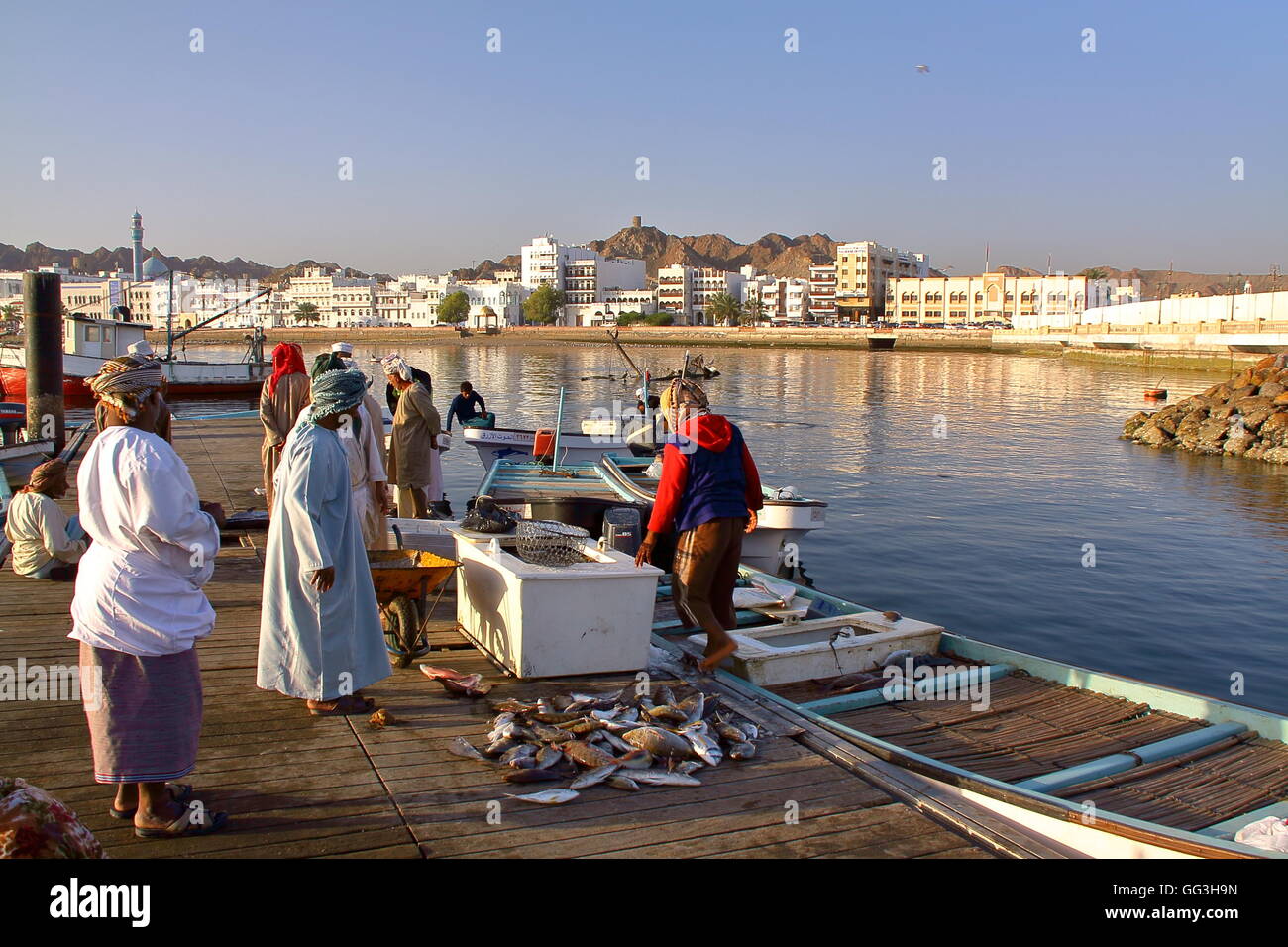 Fishermen at The Muttrah Fish docks early morning with Muttrah corniche ...