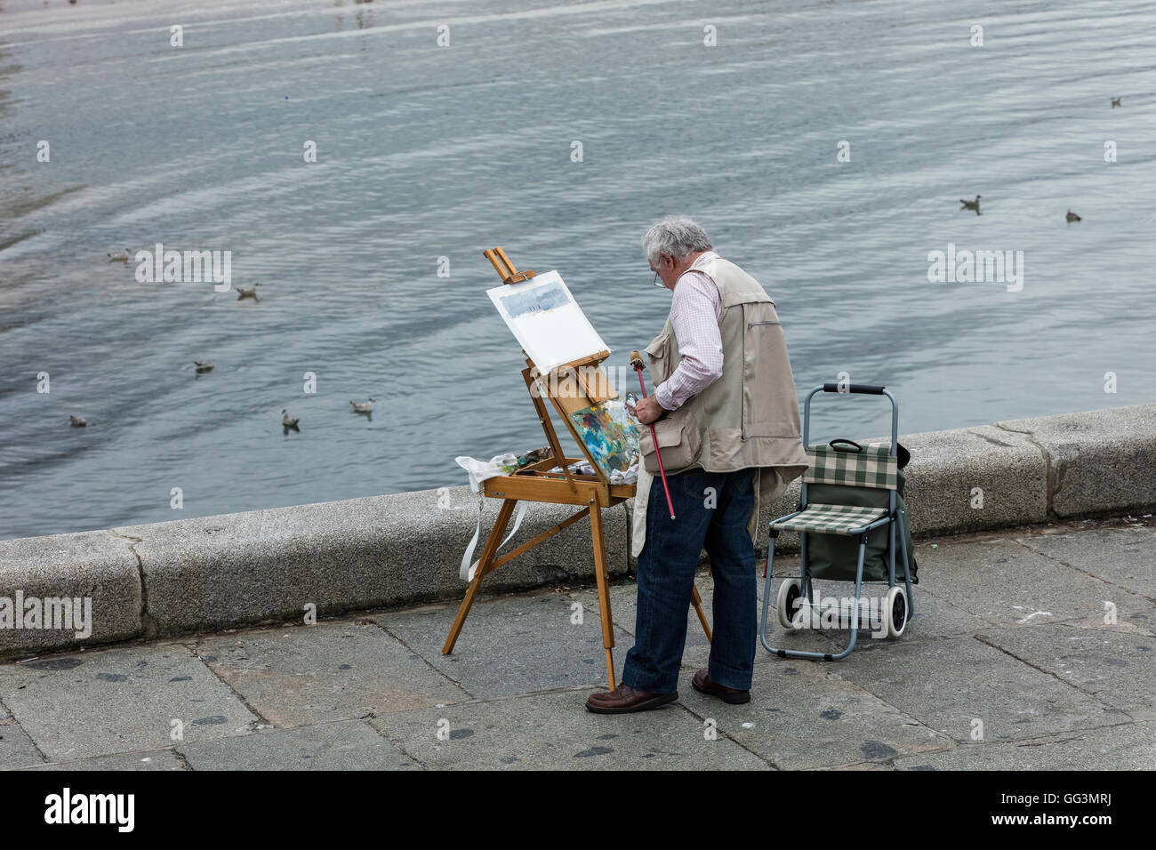 View of the back of an artist at work painting a picture oh his easel ...