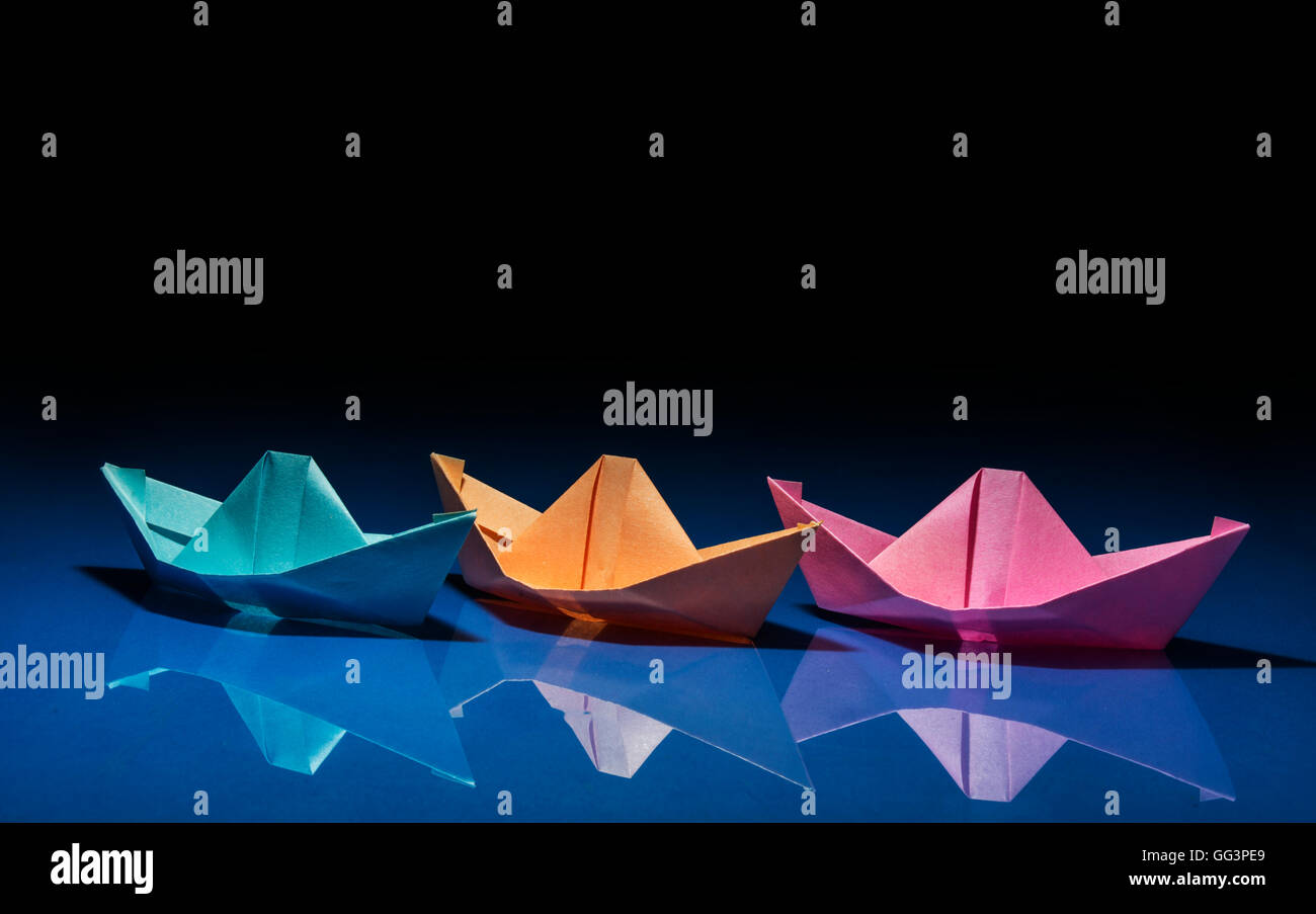 three ships of different colored paper on blue and black background ...