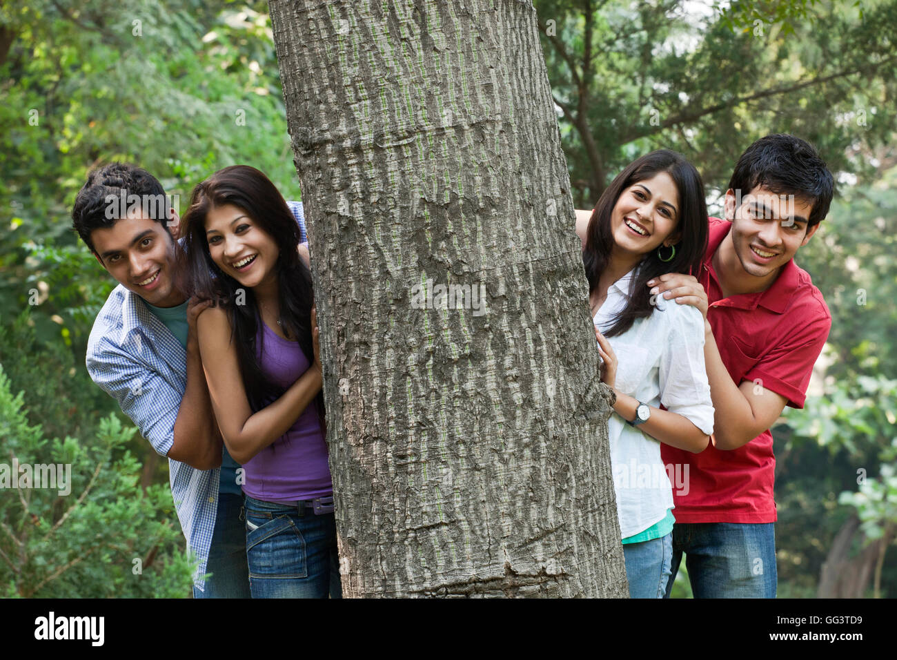 Happy college students behind tree Stock Photo - Alamy
