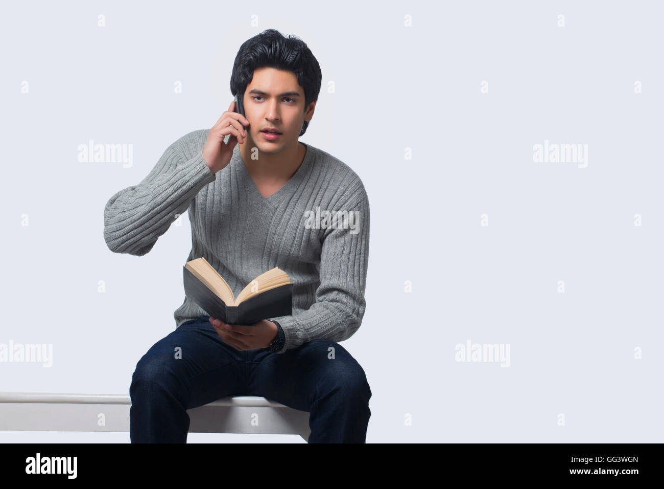 Young man holding book while talking on phone Stock Photo - Alamy