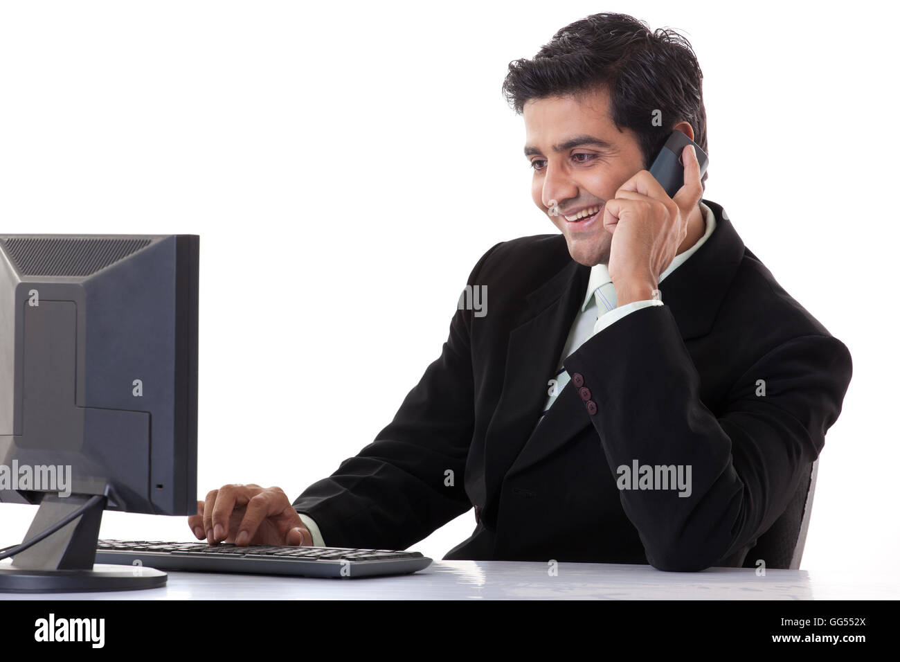 Happy smart businessman working on computer while talking on cell phone ...