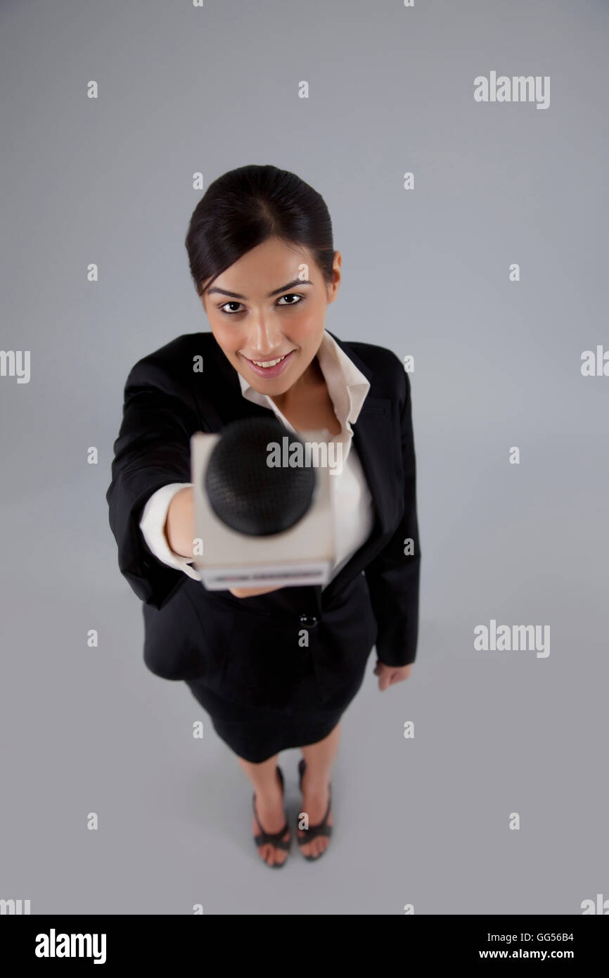 Portrait of a woman reporter holding out microphone against colored ...