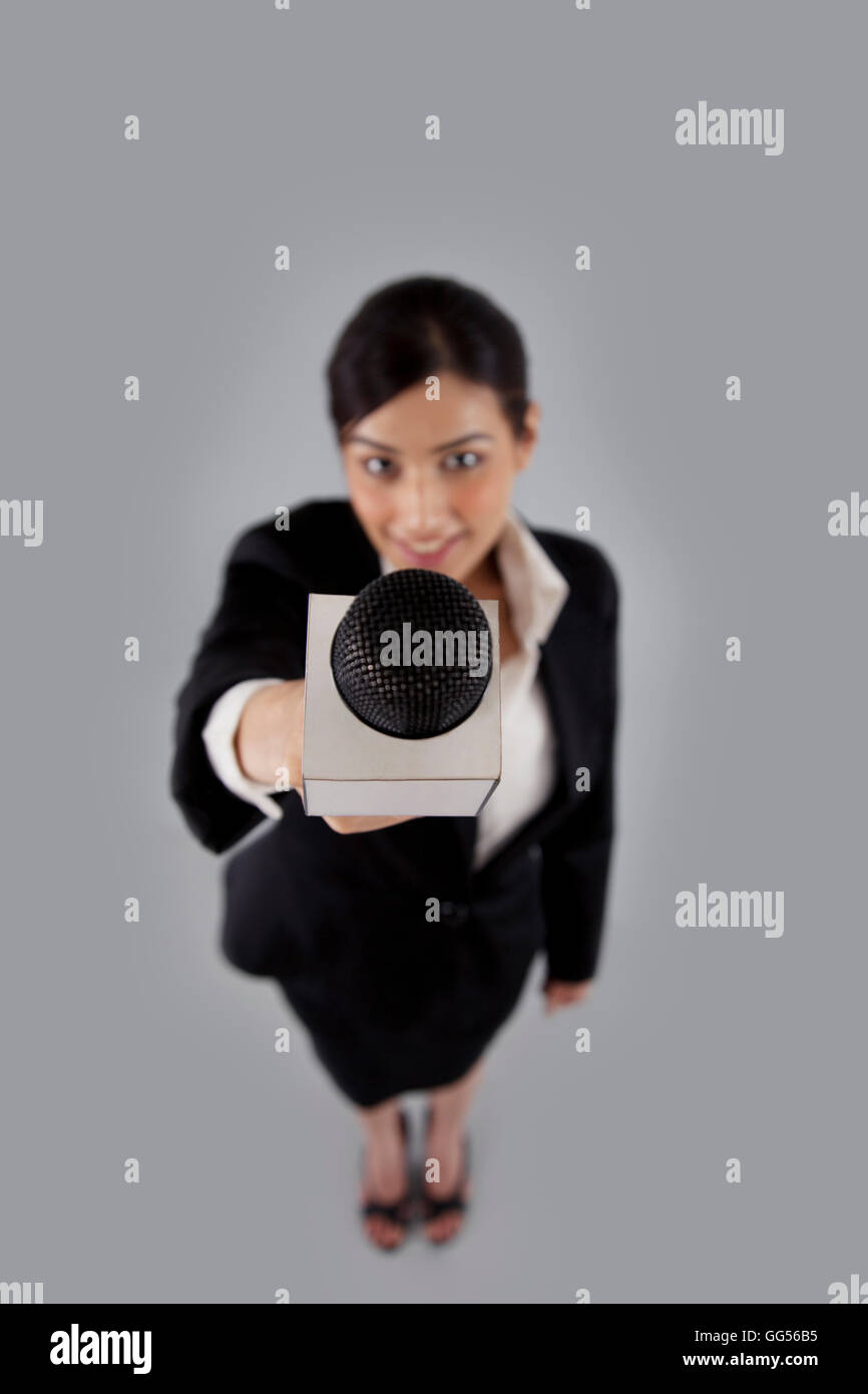 Full length of woman reporter holding out microphone against colored ...