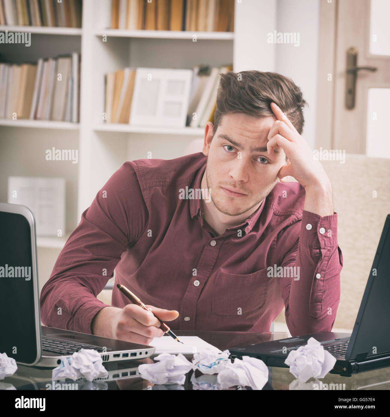 Overworked young man sitting at the desk and holding his head Stock ...