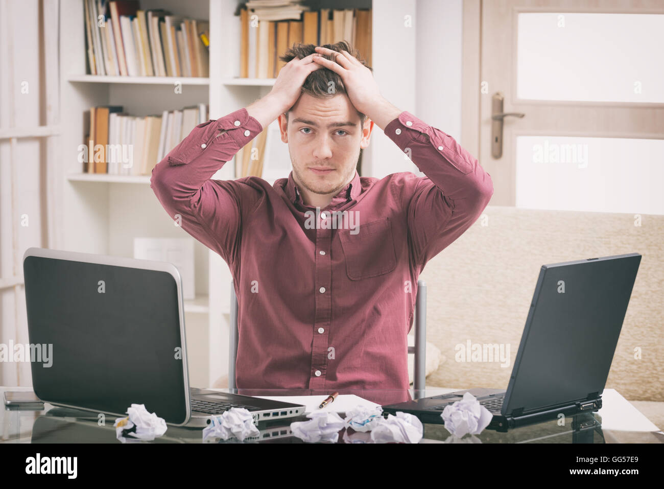 Overworked young man sitting at the desk and holding his head Stock ...