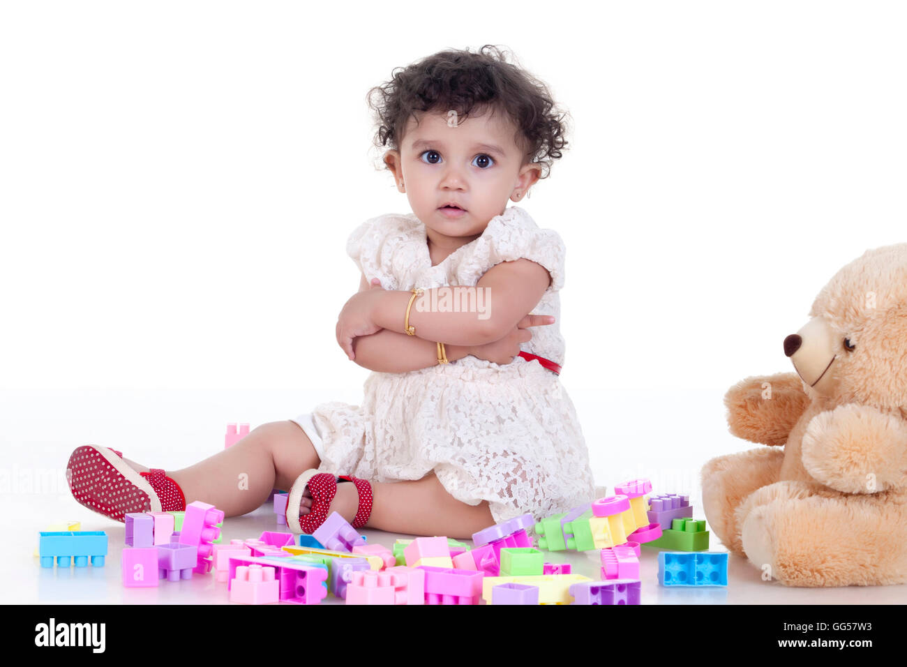 Full length of innocent girl sitting arms crossed with toys over white ...