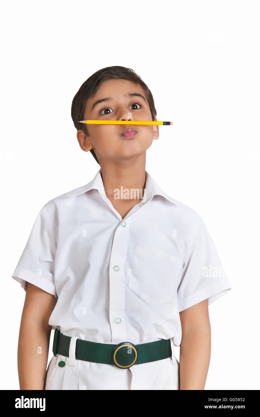 Cute boy in school uniform with pencil between nose and lips over white ...