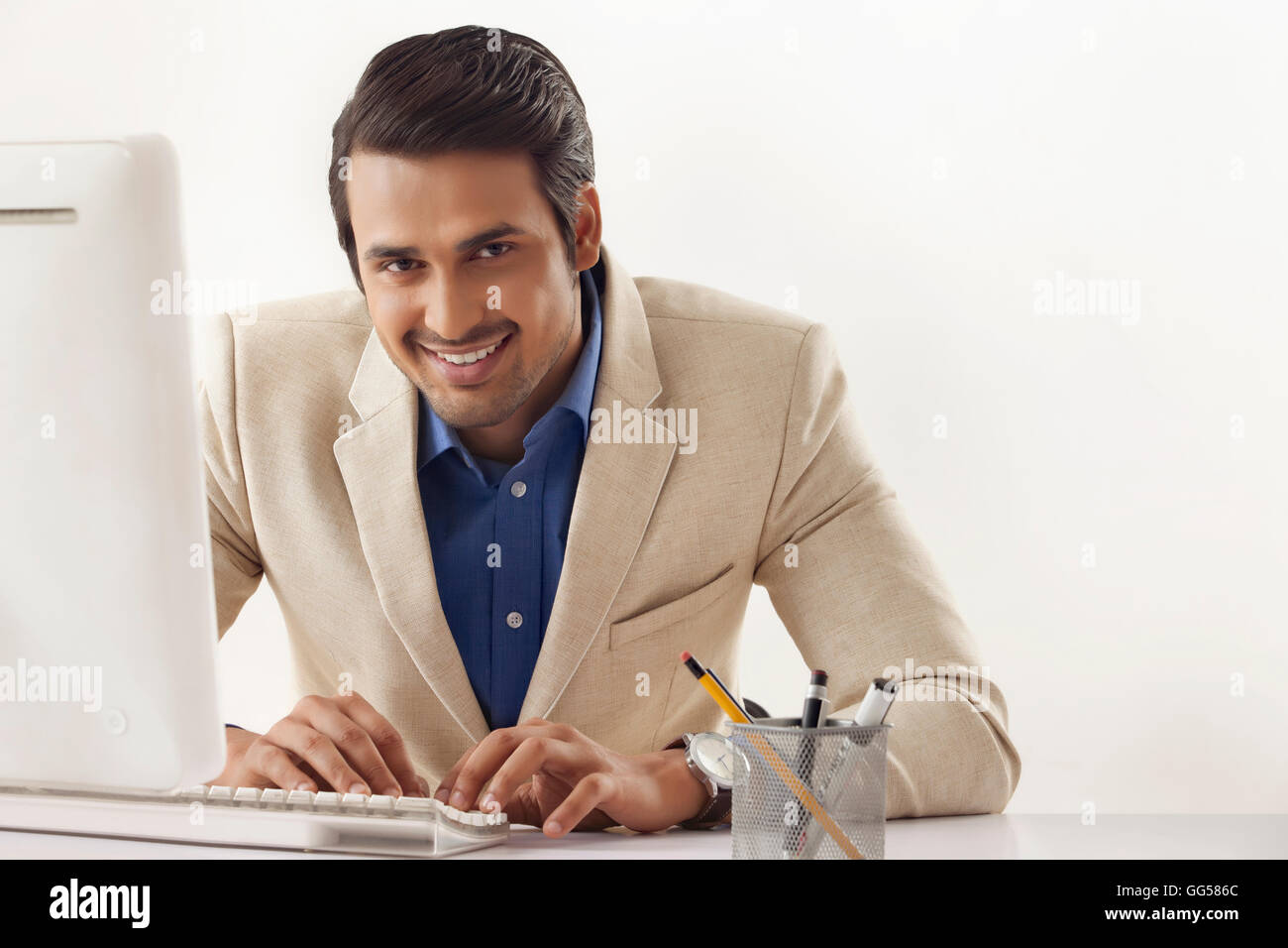 Portrait of smiling Indian businessman using computer at office desk ...
