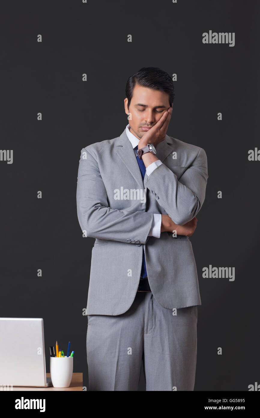 Tired businessman sleeping while standing by office desk Stock Photo ...