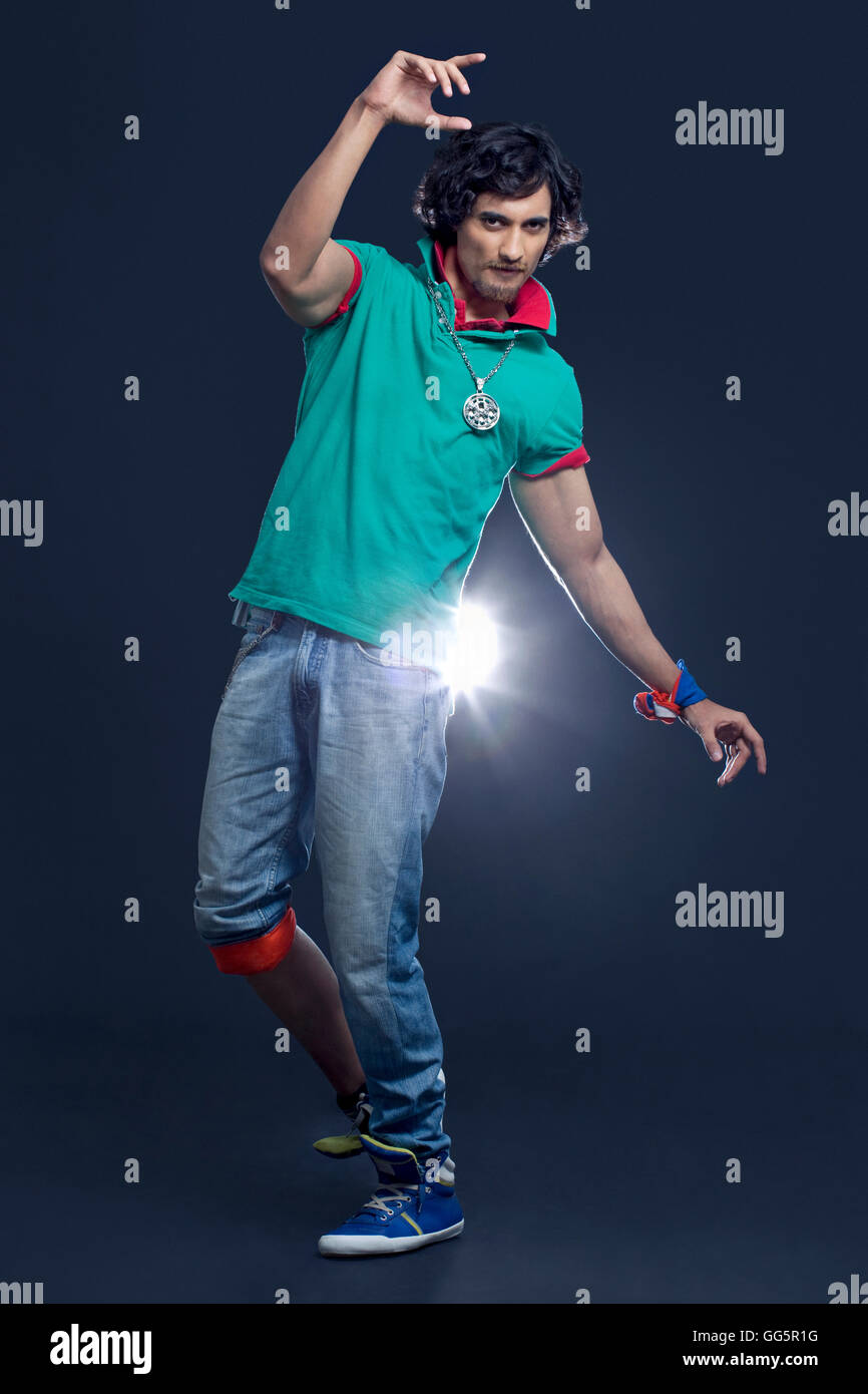 Full length of a young Indian man dancing with spotlight in background ...