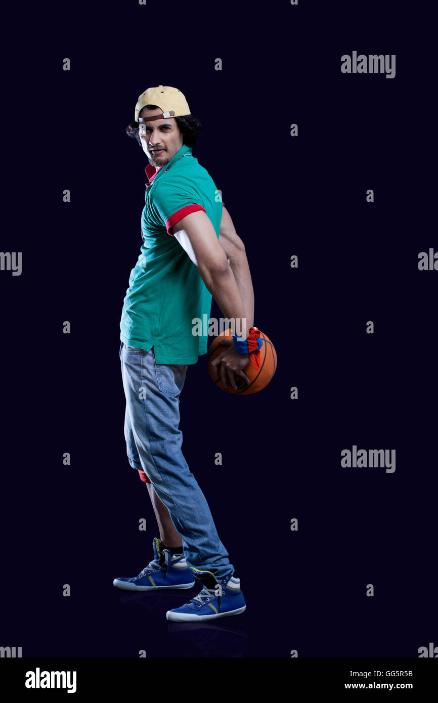 Full length of a young man holding basket ball behind his back against ...