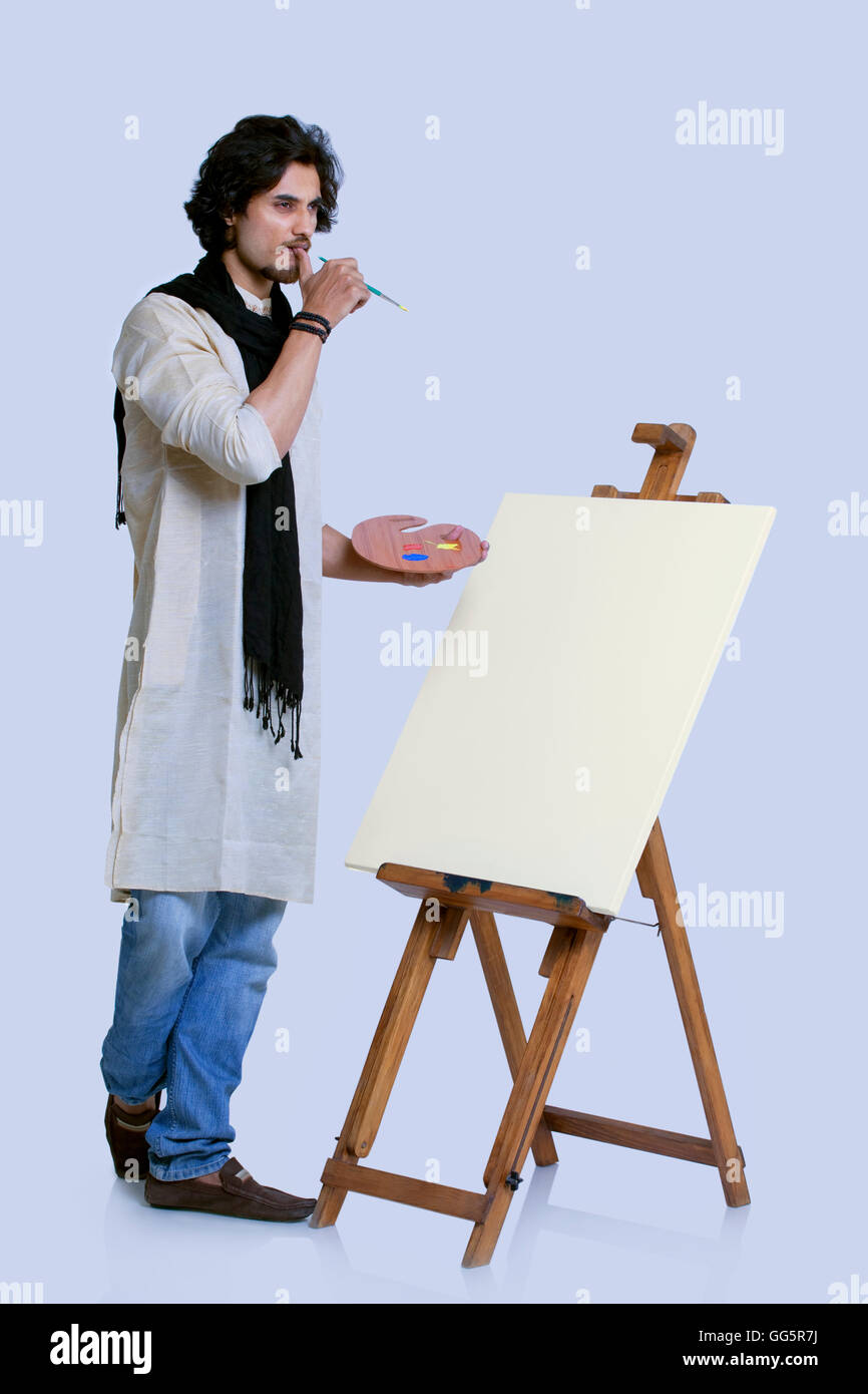 Full length of young artist contemplating against colored background ...