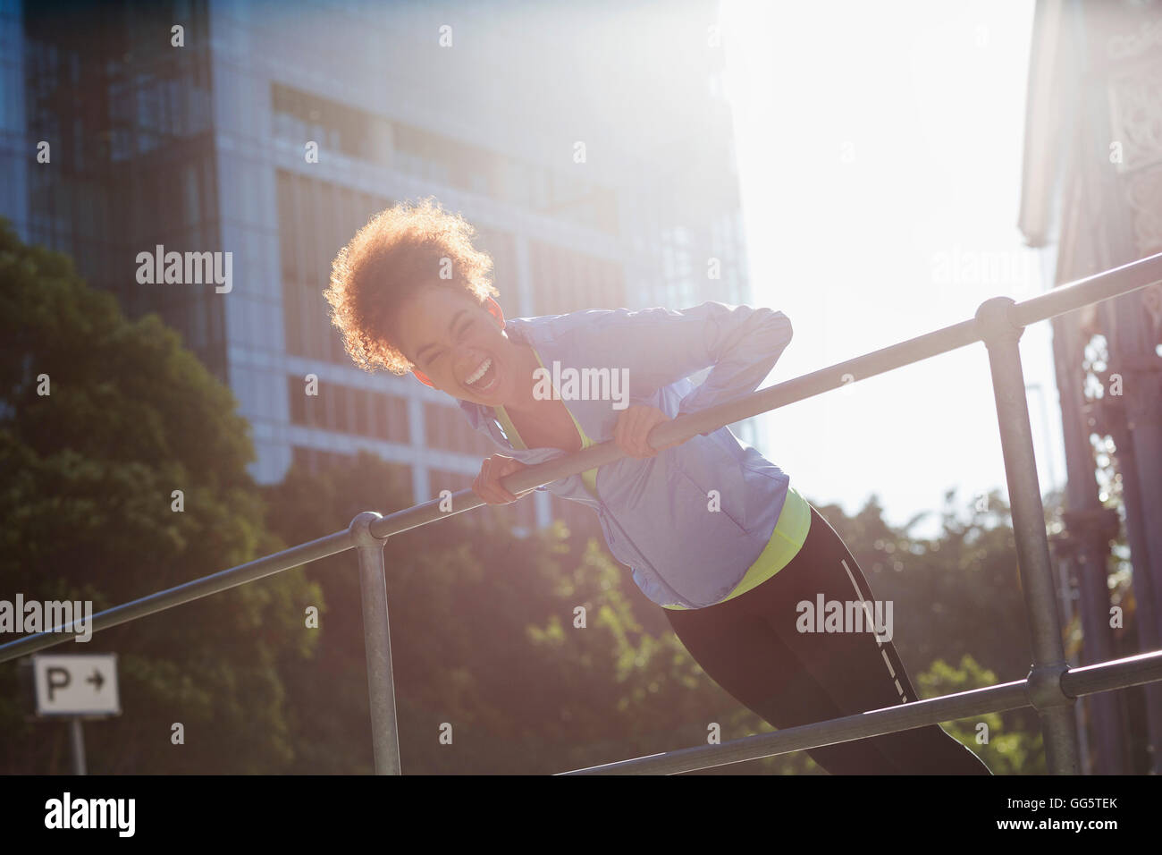 Happy young female athlete doing stretching exercise by railings on ...