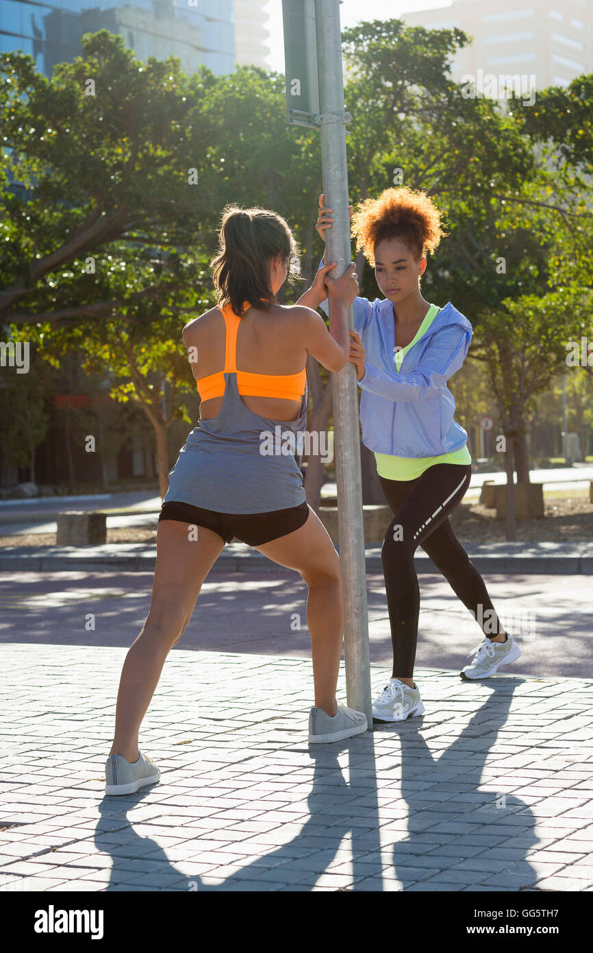 Young female athletes doing stretching exercise by pole on street Stock ...