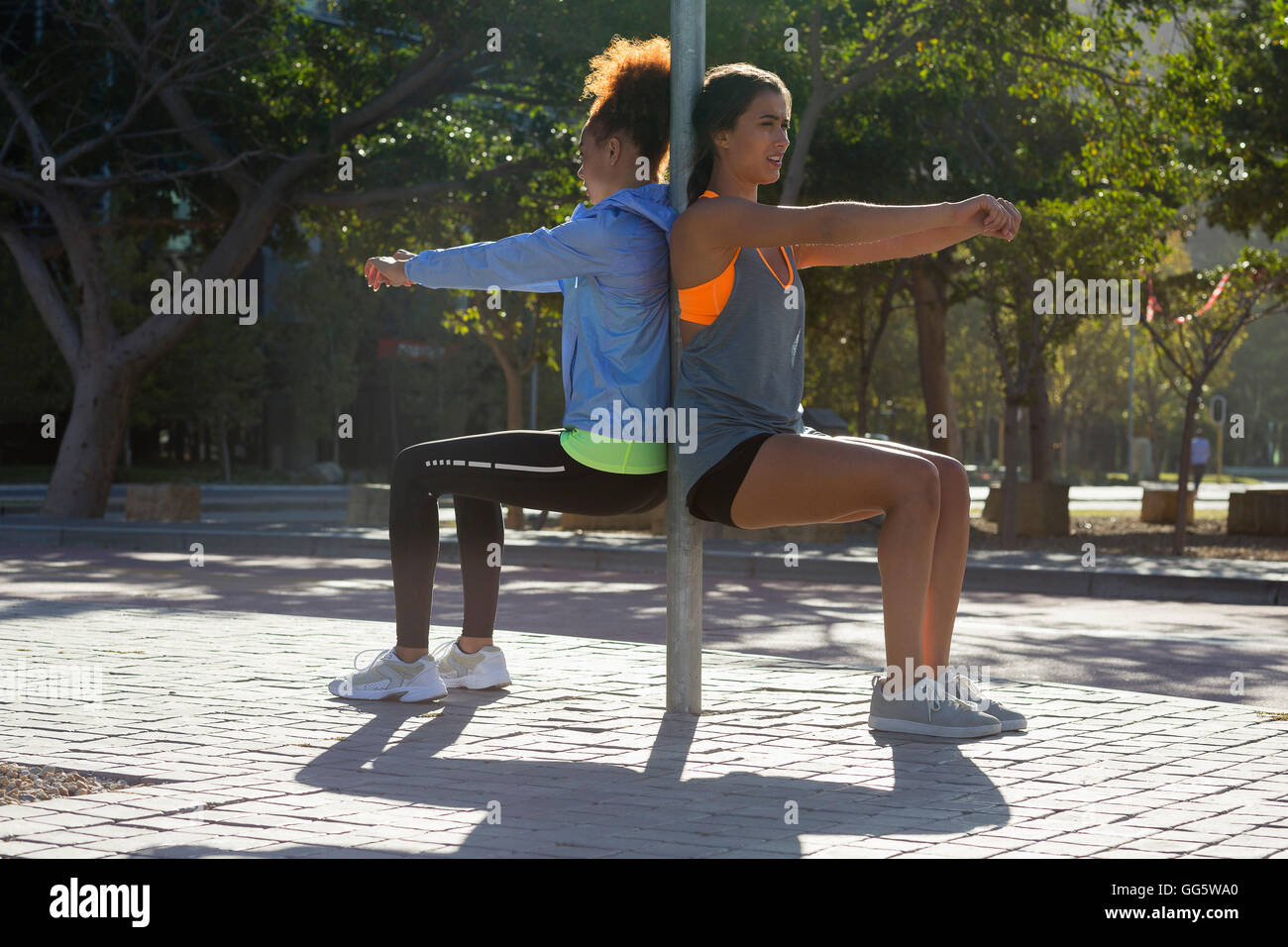 Young female athletes doing stretching exercise by pole on street Stock ...