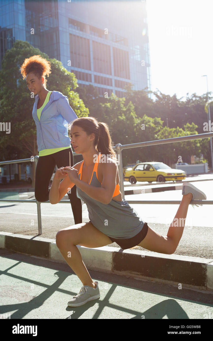 Young female athletes doing stretching exercise by railings on street ...