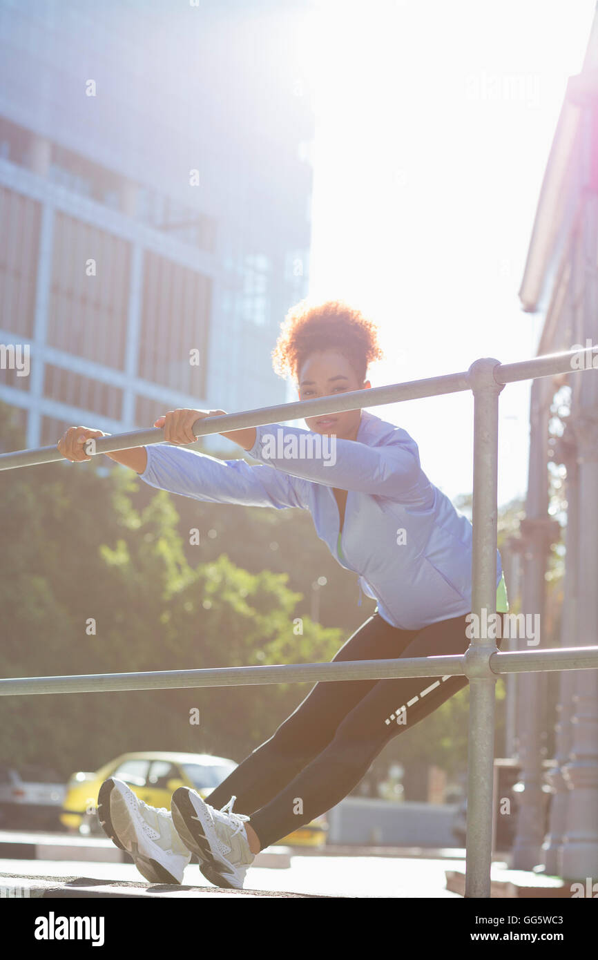 Young female athlete doing stretching exercise by railings on street ...