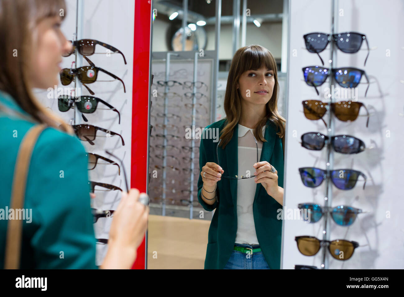 Young woman trying on eyeglasses in front of mirror in optical shop ...