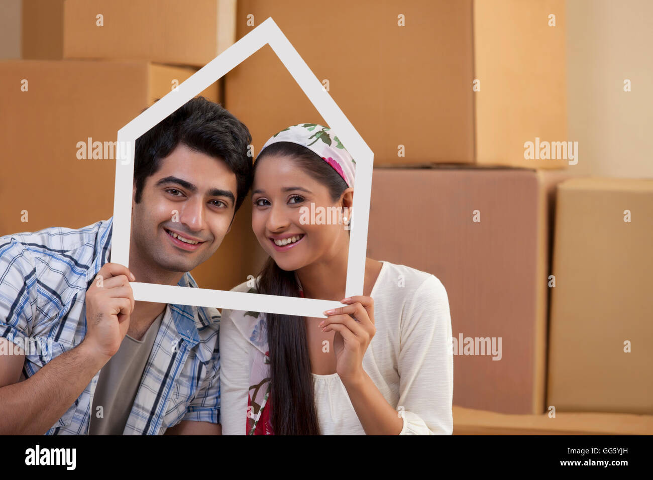 Portrait of smiling young couple looking through a house shaped frame ...