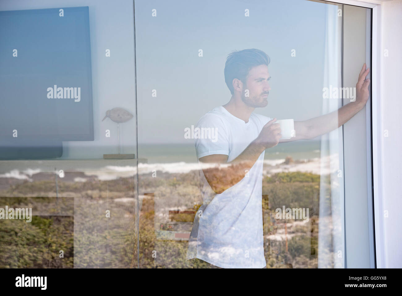 Young man looking through window with cup of coffee Stock Photo - Alamy