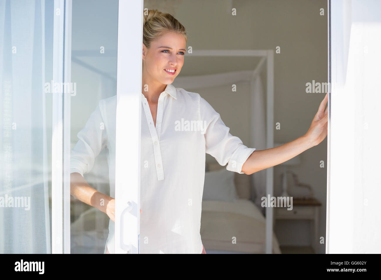 Beautiful young woman standing by window Stock Photo - Alamy