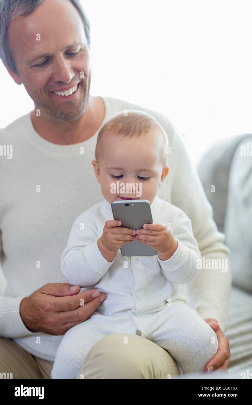Happy father and his baby daughter playing with mobile phone on couch ...