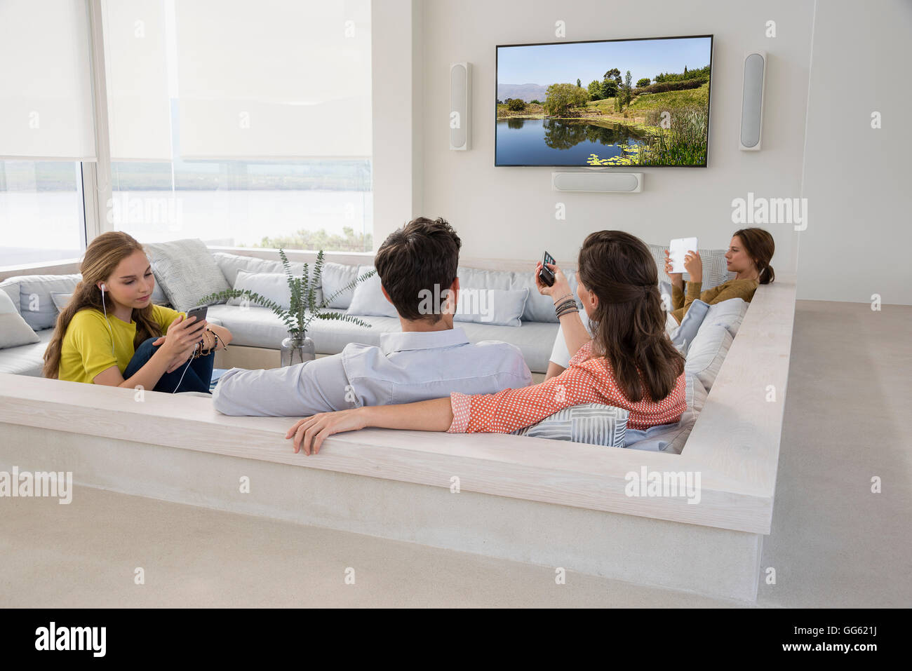 Rear view of couple watching television with their daughters busy in ...