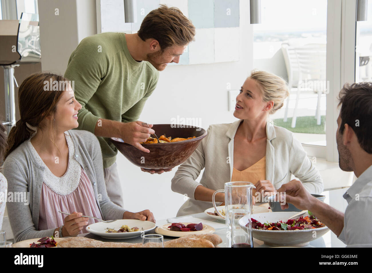 Young man serving food to her friends at dining table Stock Photo - Alamy