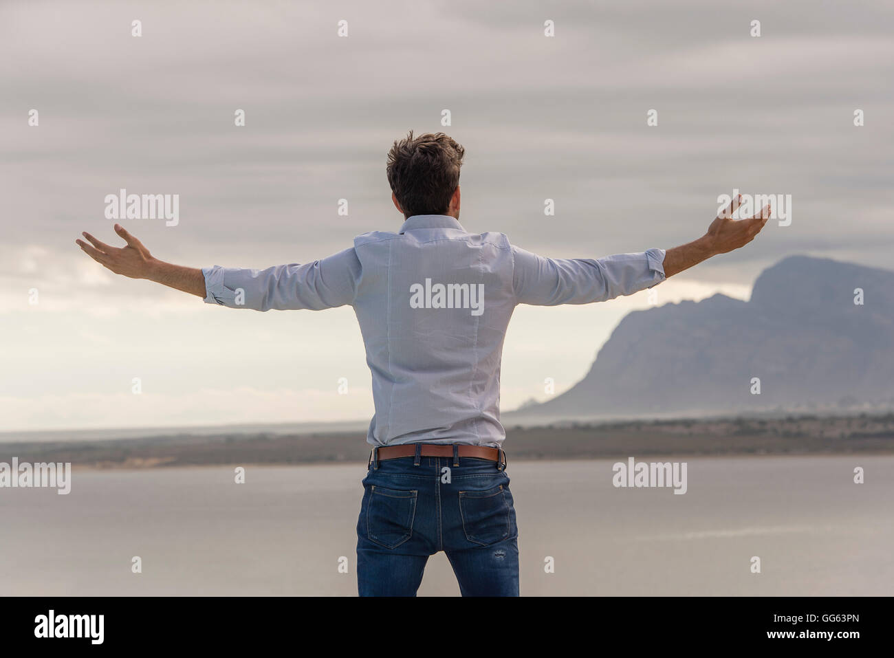 Rear view of a man standing at lakeshore with his arm outstretched ...