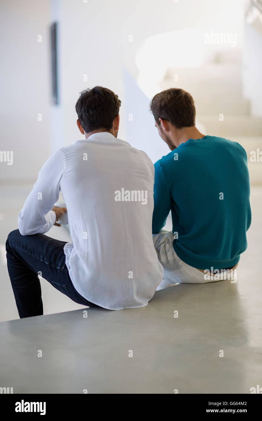 Rear view of two male friends sitting on the floor Stock Photo - Alamy