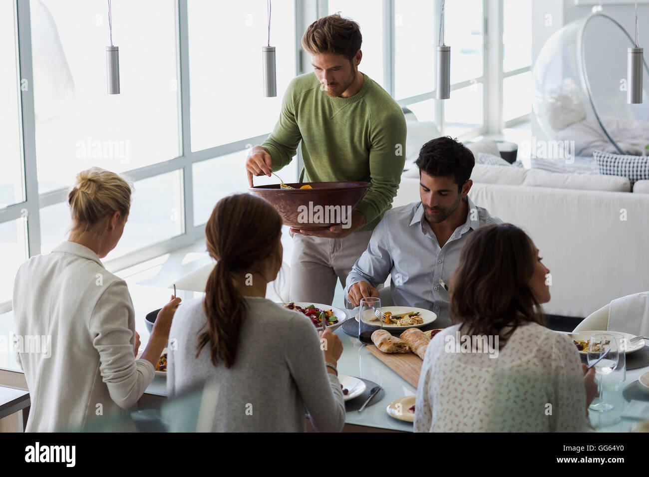 Young man serving food to his friends at dining table Stock Photo - Alamy