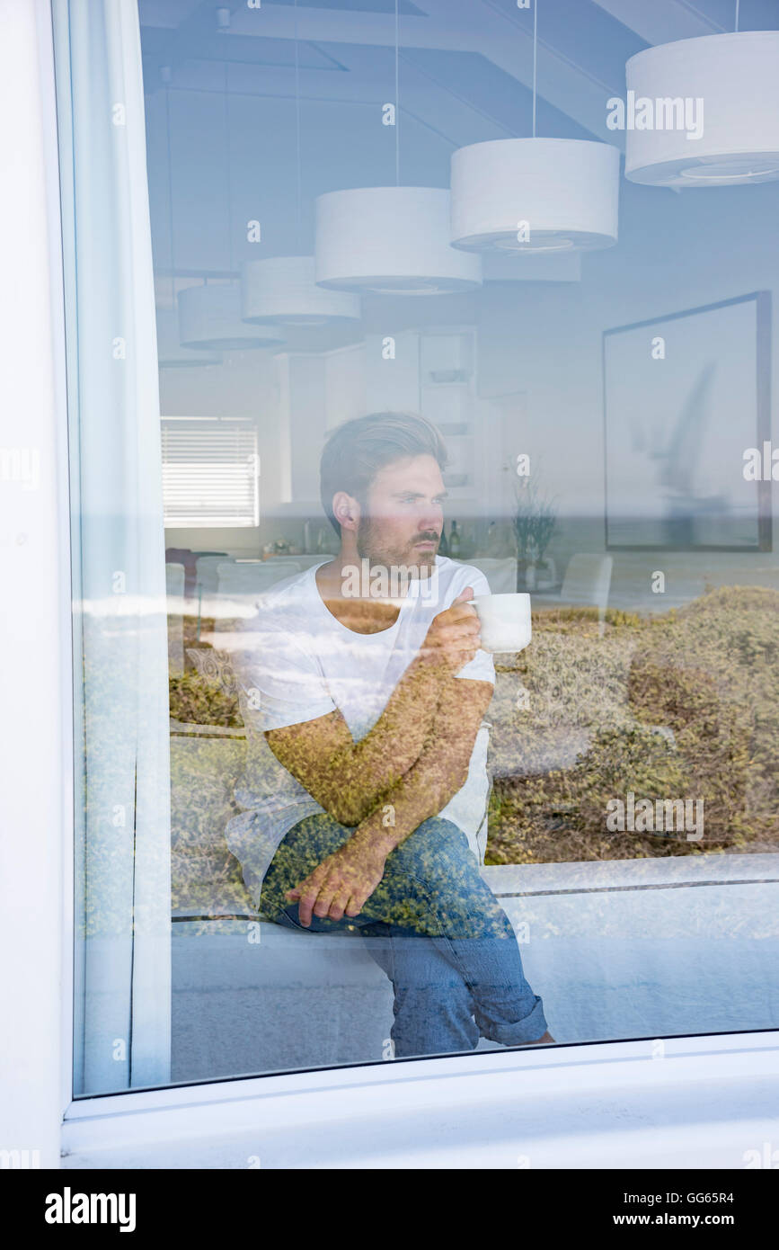 Young man looking through window with cup of coffee Stock Photo - Alamy