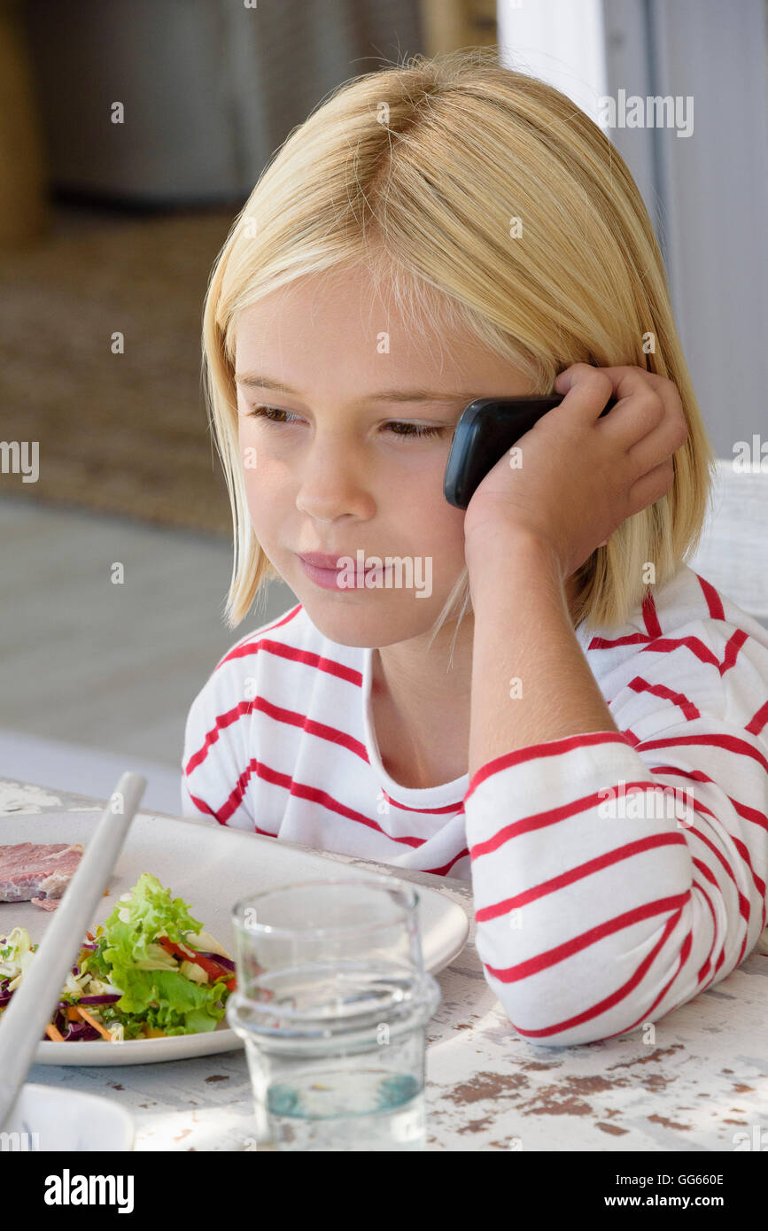 Little girl talking on mobile phone while eating meal Stock Photo - Alamy