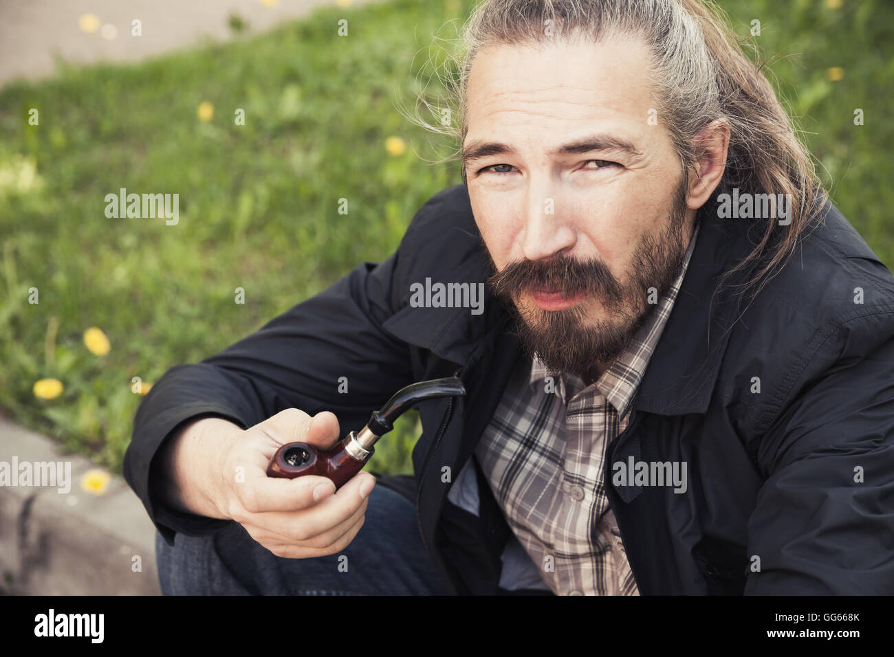 Asian man smoking a pipe on green grass in park, close-up photo with ...