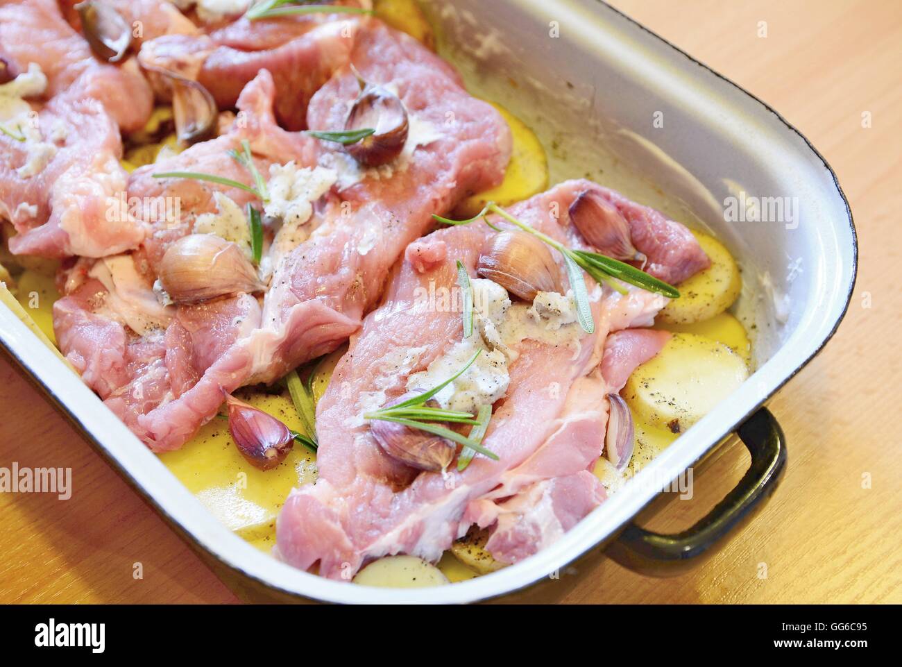 Raw pork neck chops with potatoes slices, rosemary and garlic in pan ...