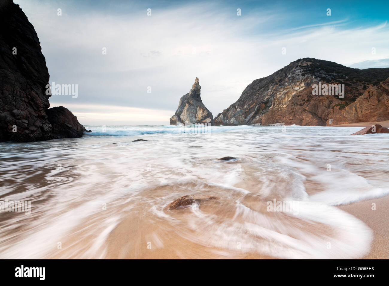 Ocean waves crashing on the sandy beach of Praia da Ursa surrounded by ...