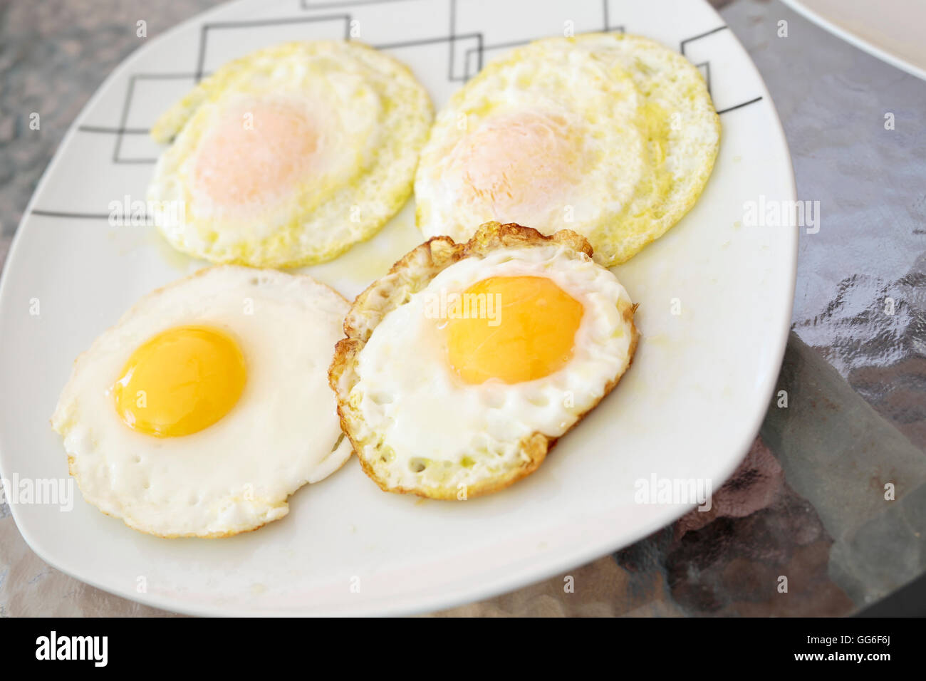 Four fried eggs on a plate on a glass table Stock Photo - Alamy