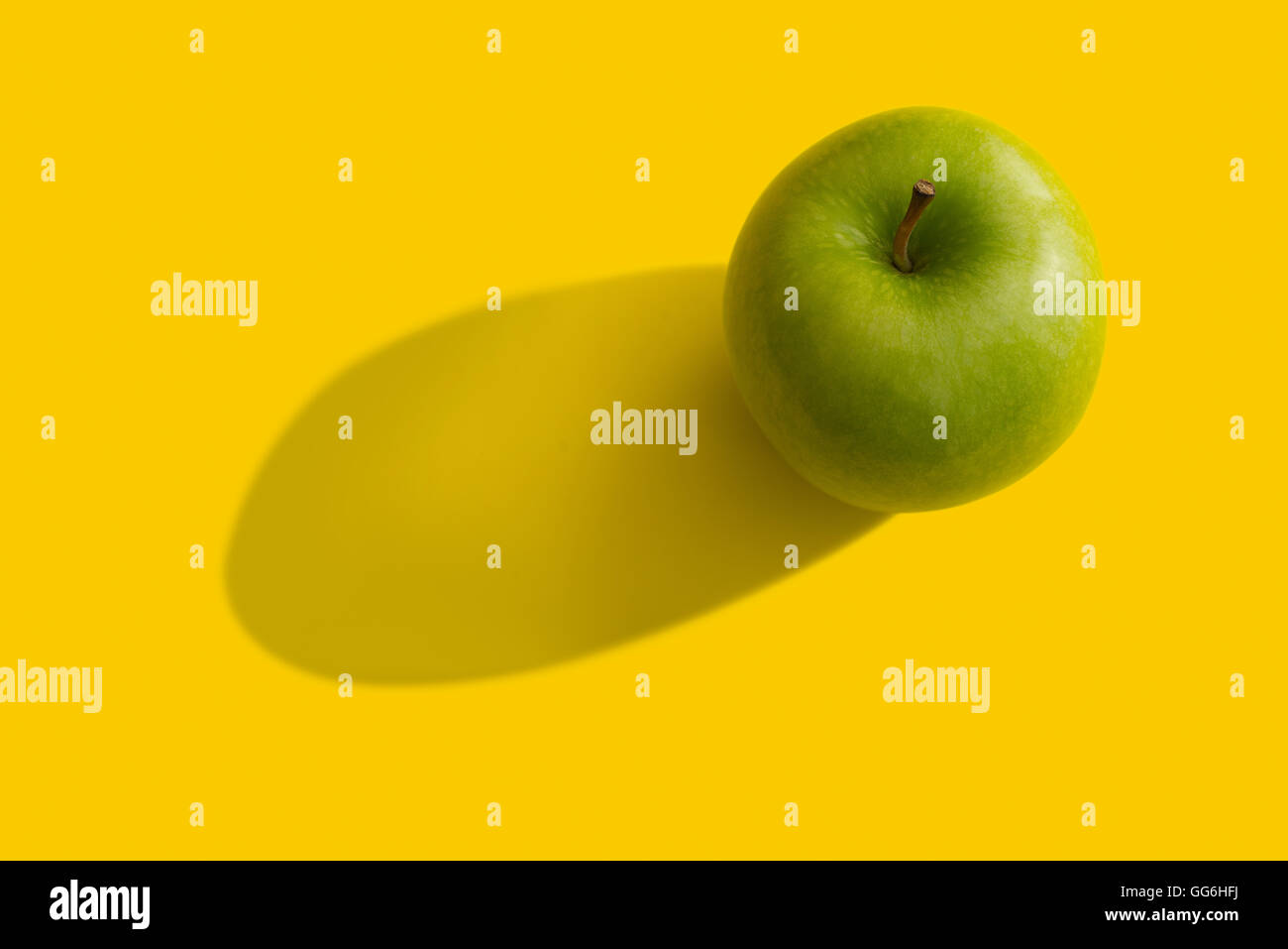Green apple with shadow over yellow background Stock Photo - Alamy