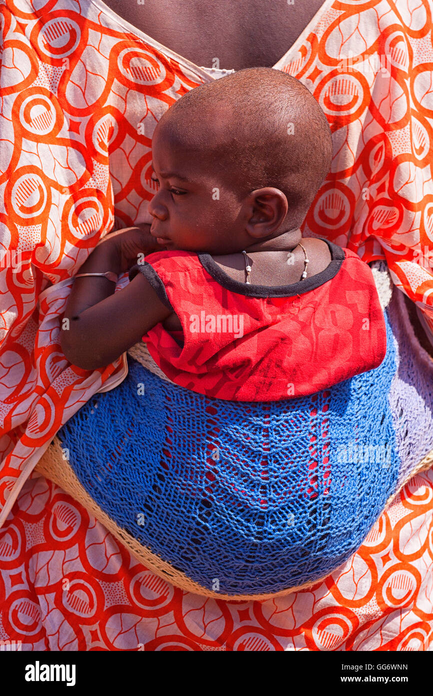 African bedik woman carrying a child while doing housework, ziguinchor ...