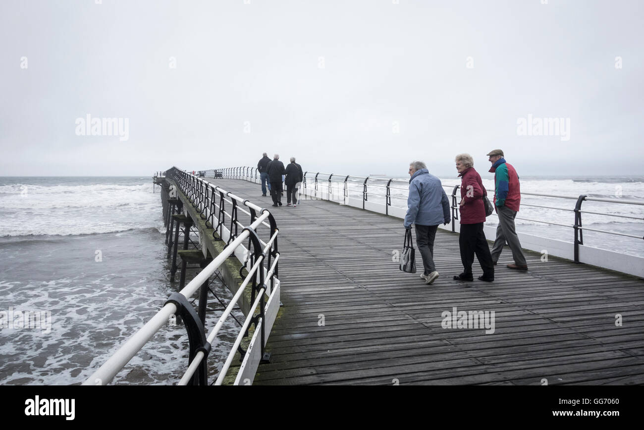 Elderly people walking on Saltburn`s Victorian pier on a cold, grey ...