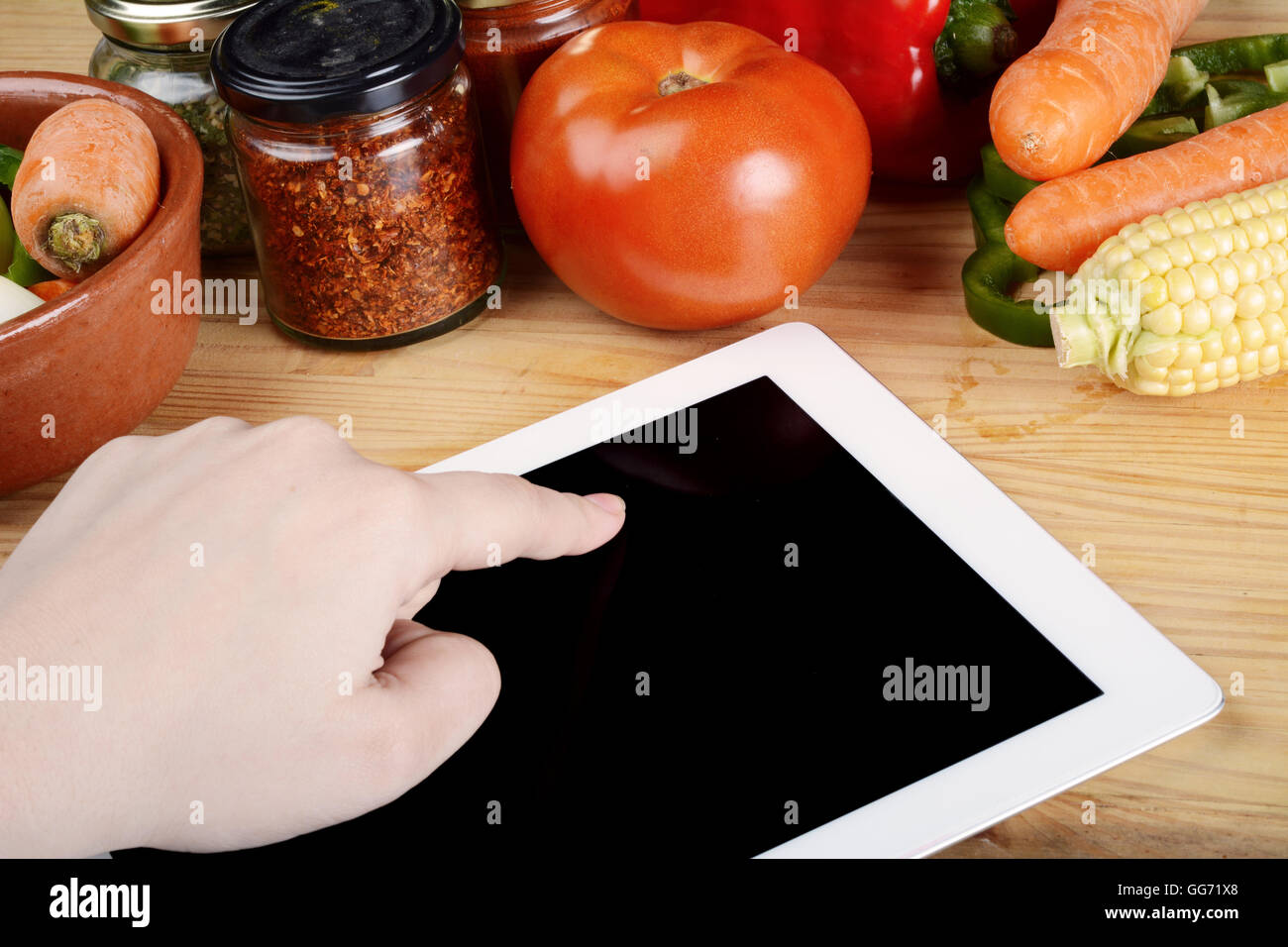 Person preparing food from recipe on tablet with vegetables and spices ...