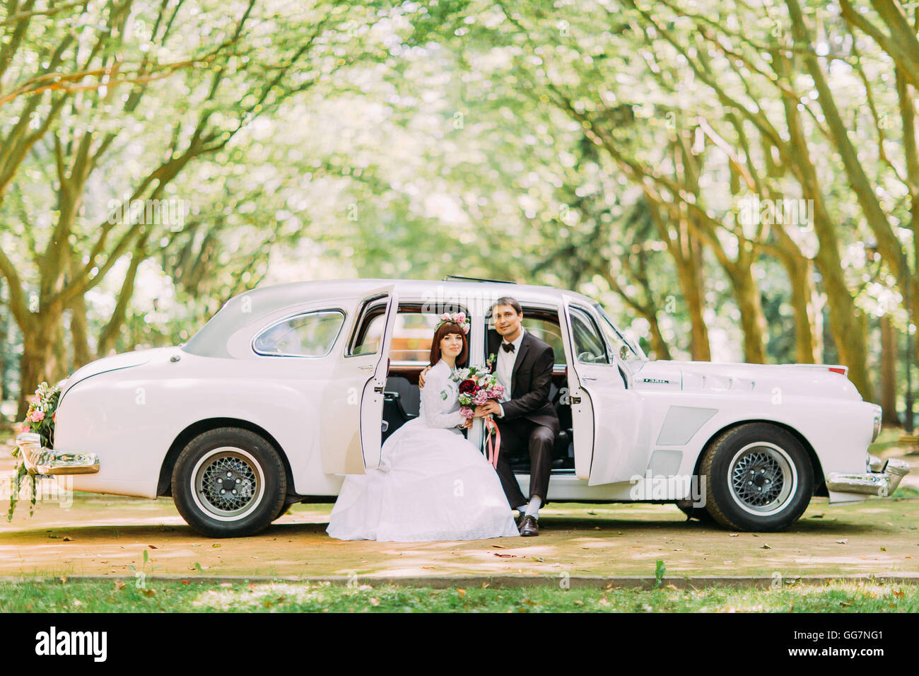 Charming bride and groom sitting in retro car at their wedding day ...