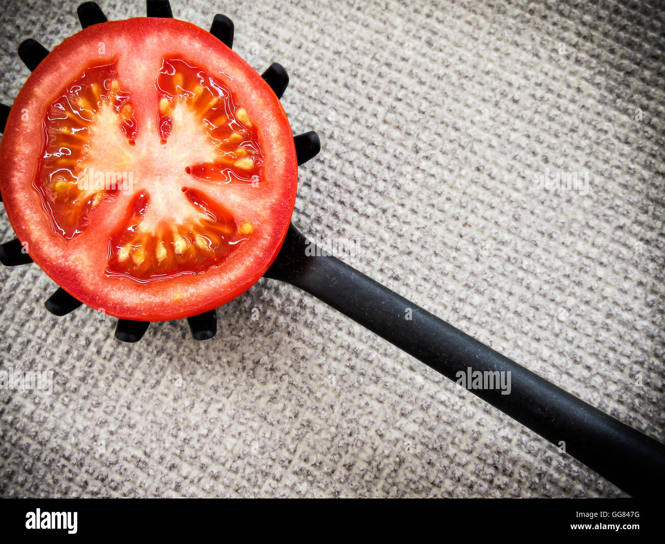 Half tomato on a toothed kitchen spoon on a gray ground. Horizontal ...