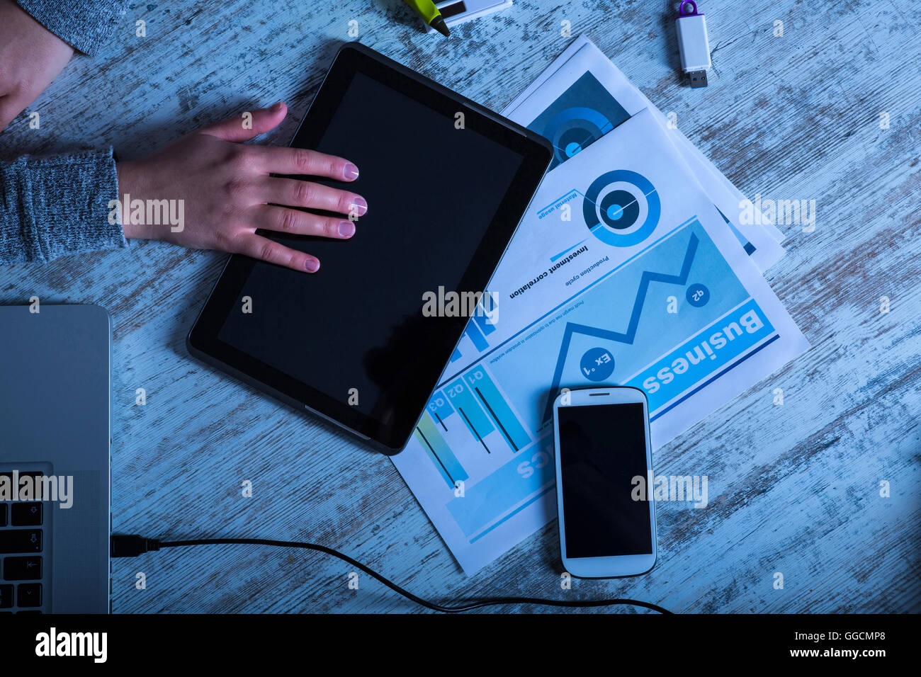 A working woman’s hand at night at a table with laptop, tablet and ...