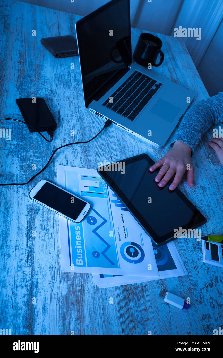 A working woman’s hand at night at a table with laptop, tablet and ...