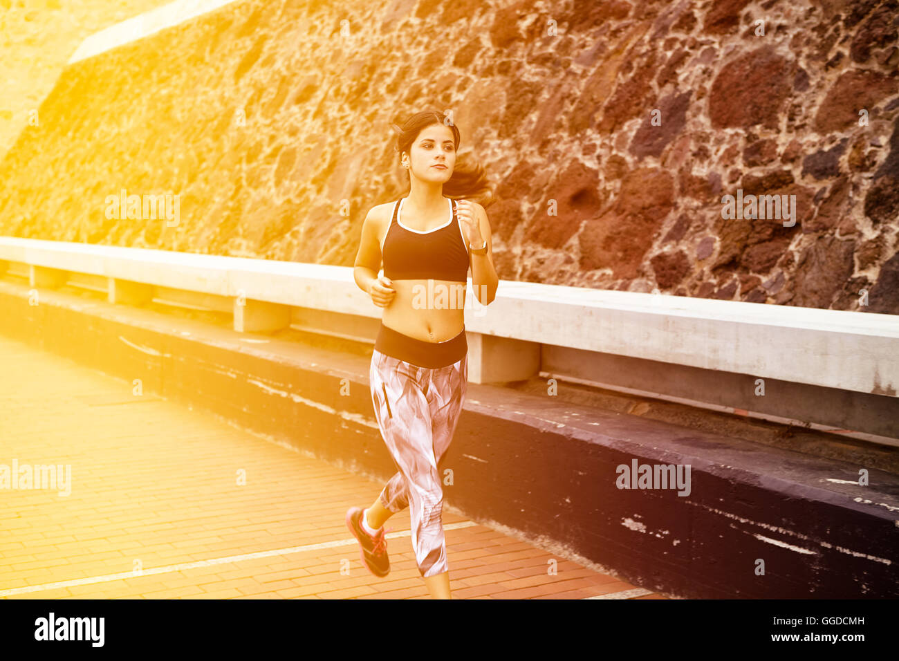 Young girl jogging on a paved road next to a rock wall barrier, wearing ...