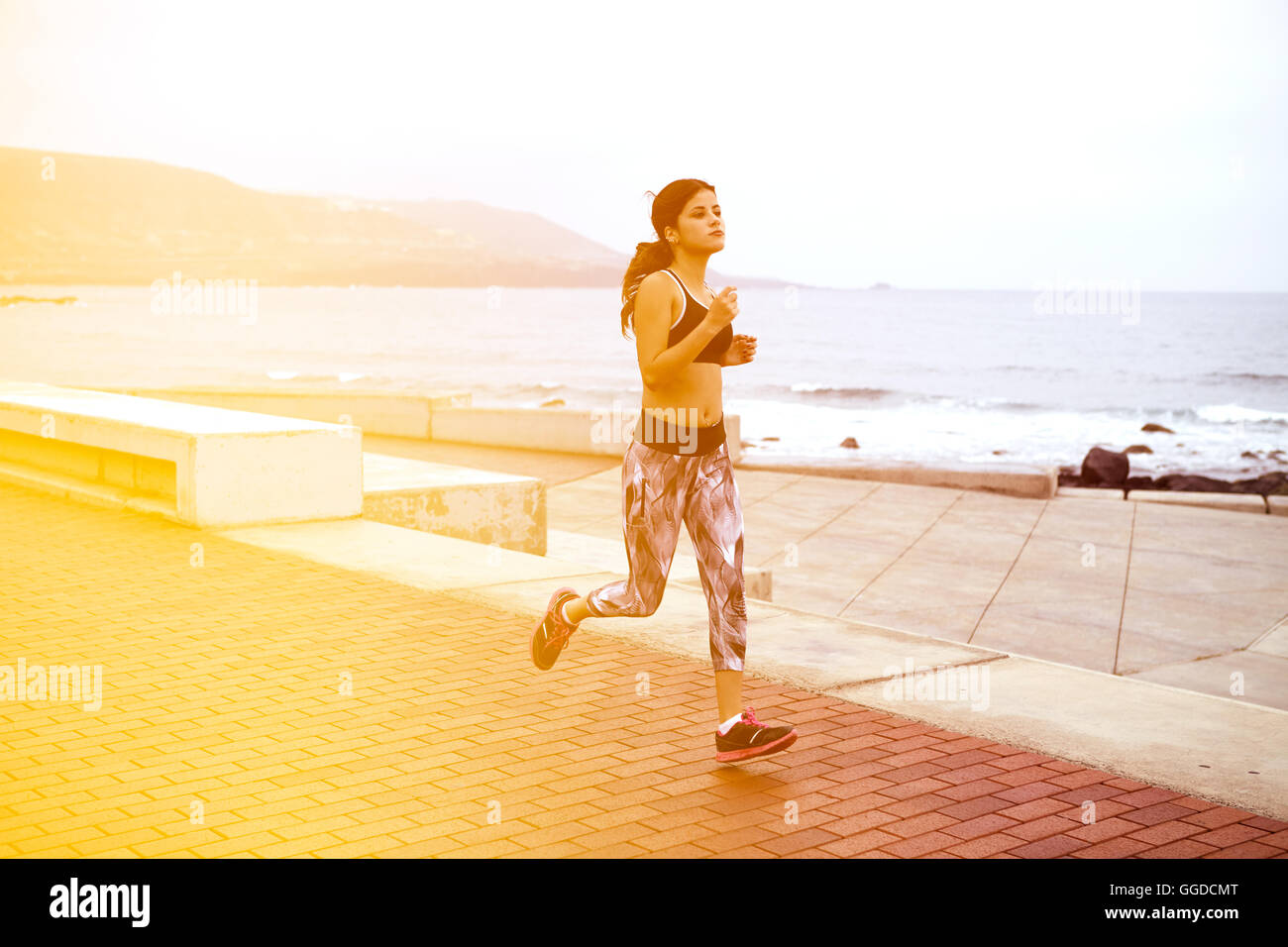 Young girl jogging on a paved esplanade close to a seashore, wearing ...