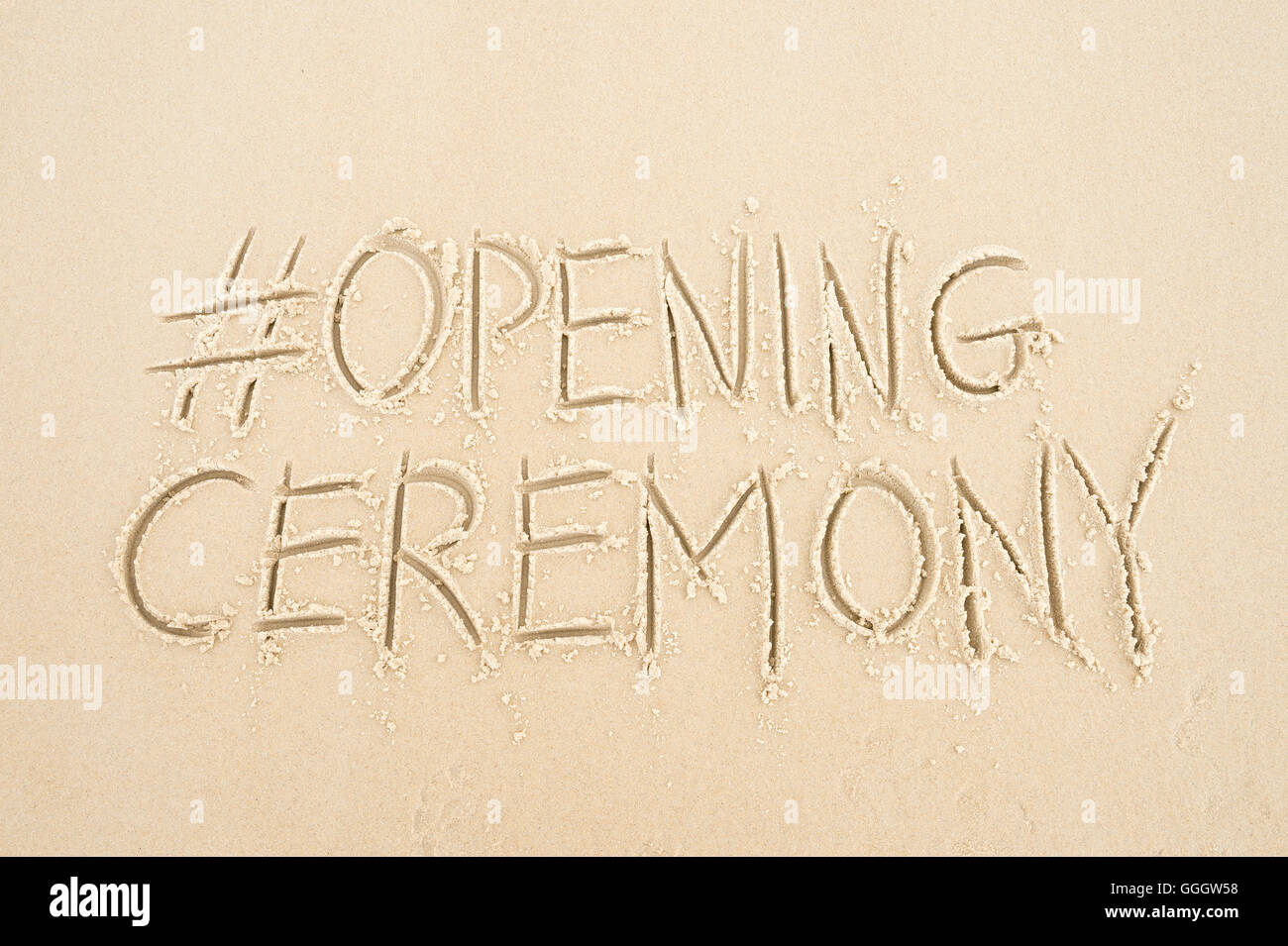 Simple hashtag Opening Ceremony message handwritten on smooth sand ...